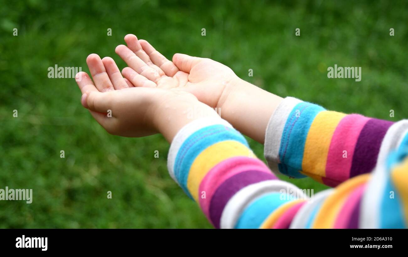 Wet baby hands in rainbow striped sleeve shirt. Kid plays in drizzle ...