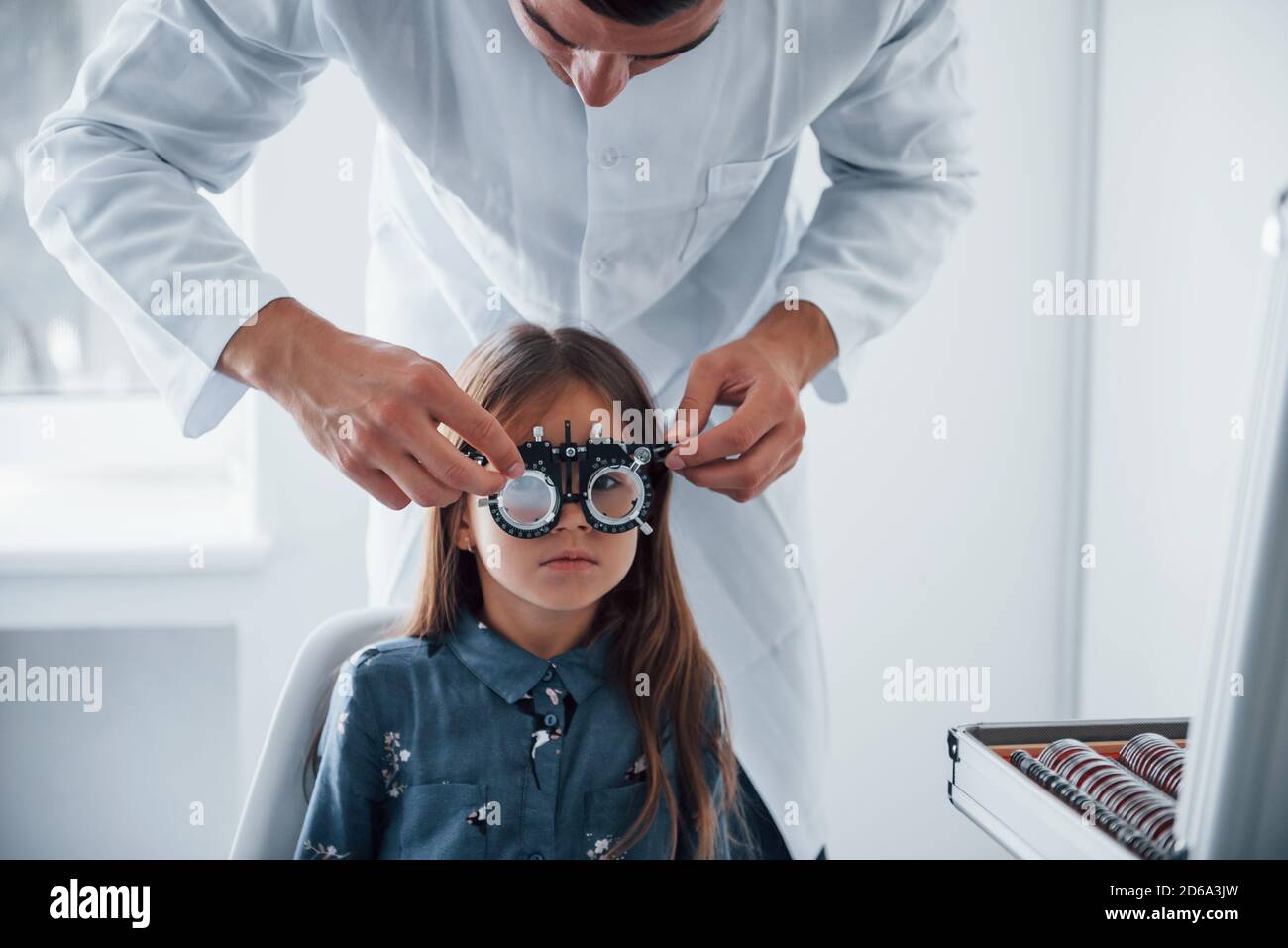 Wearing diopter. Young ophthalmologist is with little female visitor in ...