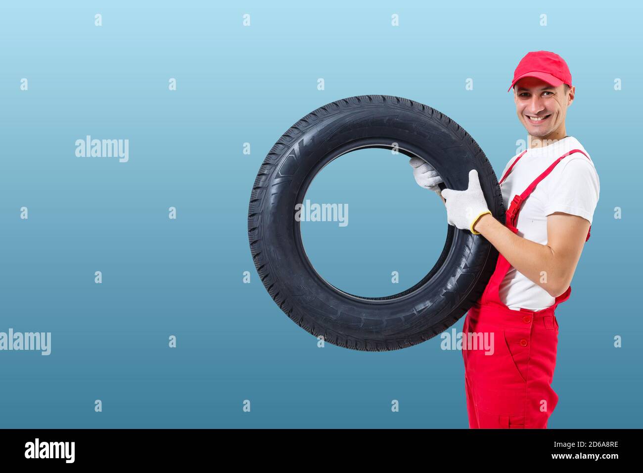 car mechanic carrying tire on blue background. happy man smiling amd ...