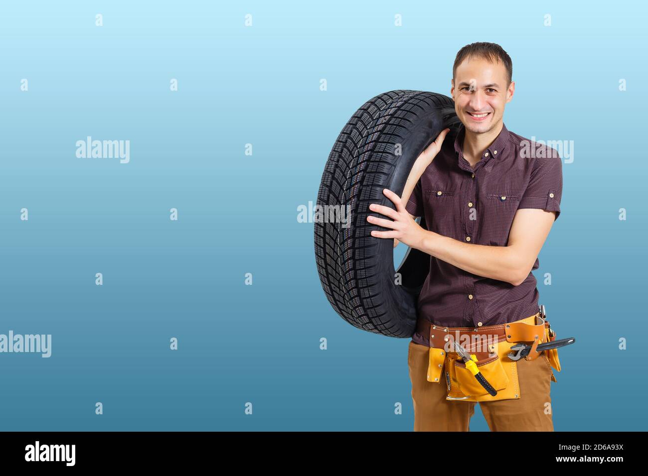 car mechanic carrying tire on blue background. happy man smiling amd ...