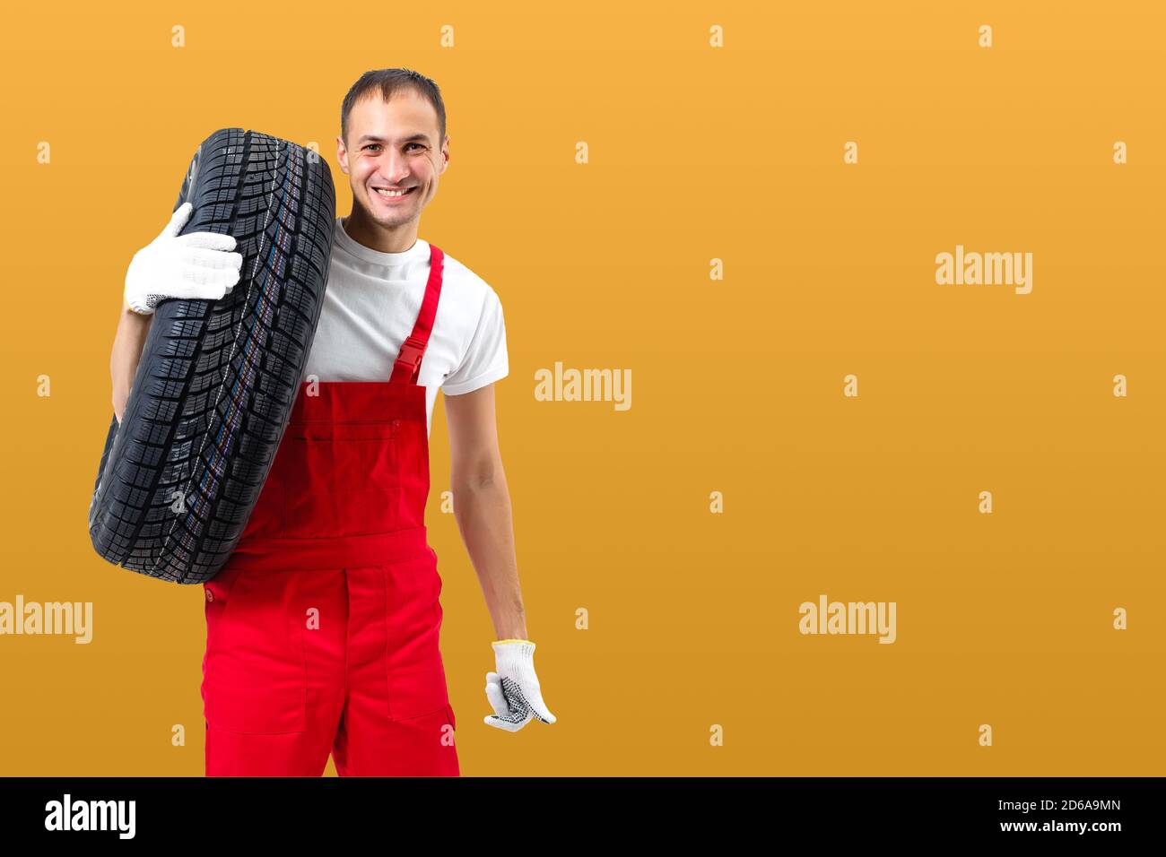 car mechanic carrying tire on yellow background. happy man smiling amd ...