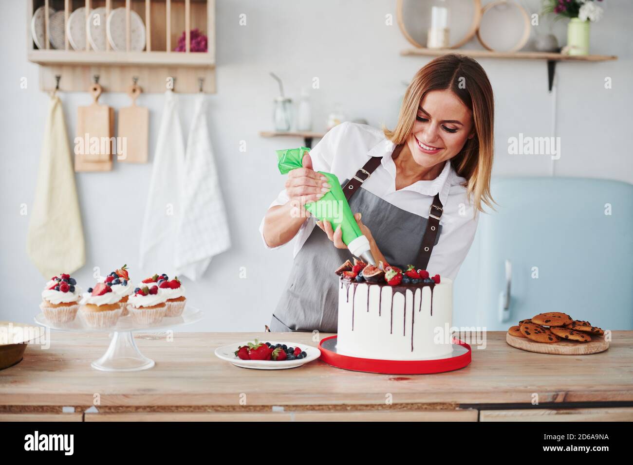 Pouring cream. Woman stands indoors in the kitchen with homemade pie ...