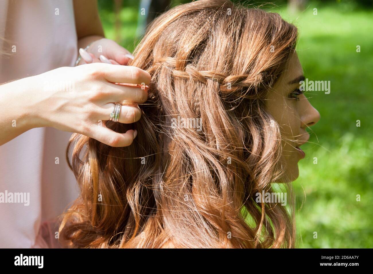 Hairstylist braiding pigtails to young girl outdoor. Creating braids ...