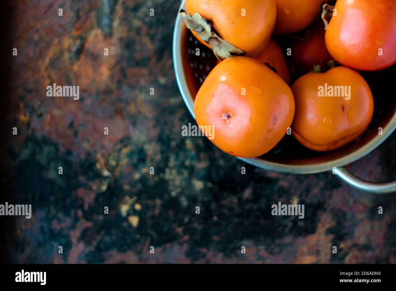 Group of persimmons in metal collander over rustic surface Stock Photo ...