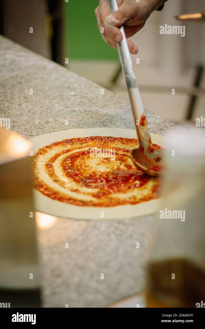 Chef smears red sauce while making the pizza Stock Photo - Alamy