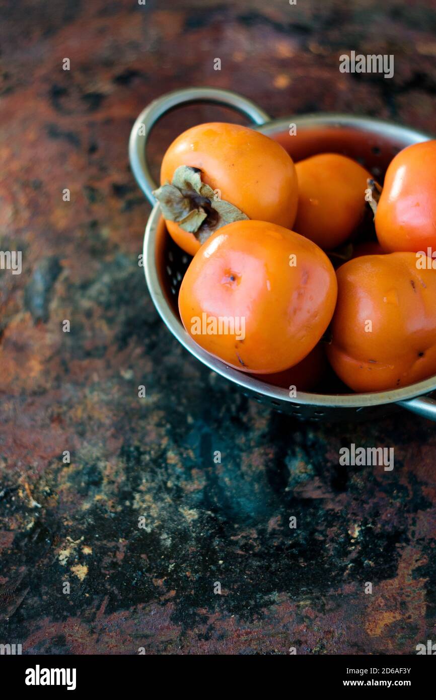 Group of persimmons in metal collander over rustic surface Stock Photo ...