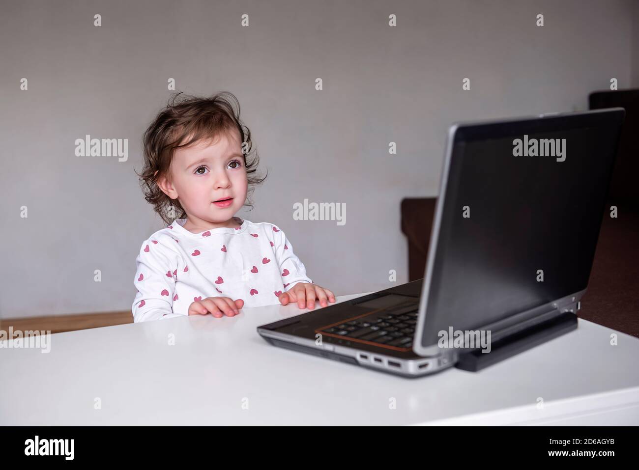 A charming little girl sits behind laptop, learns from distance ...