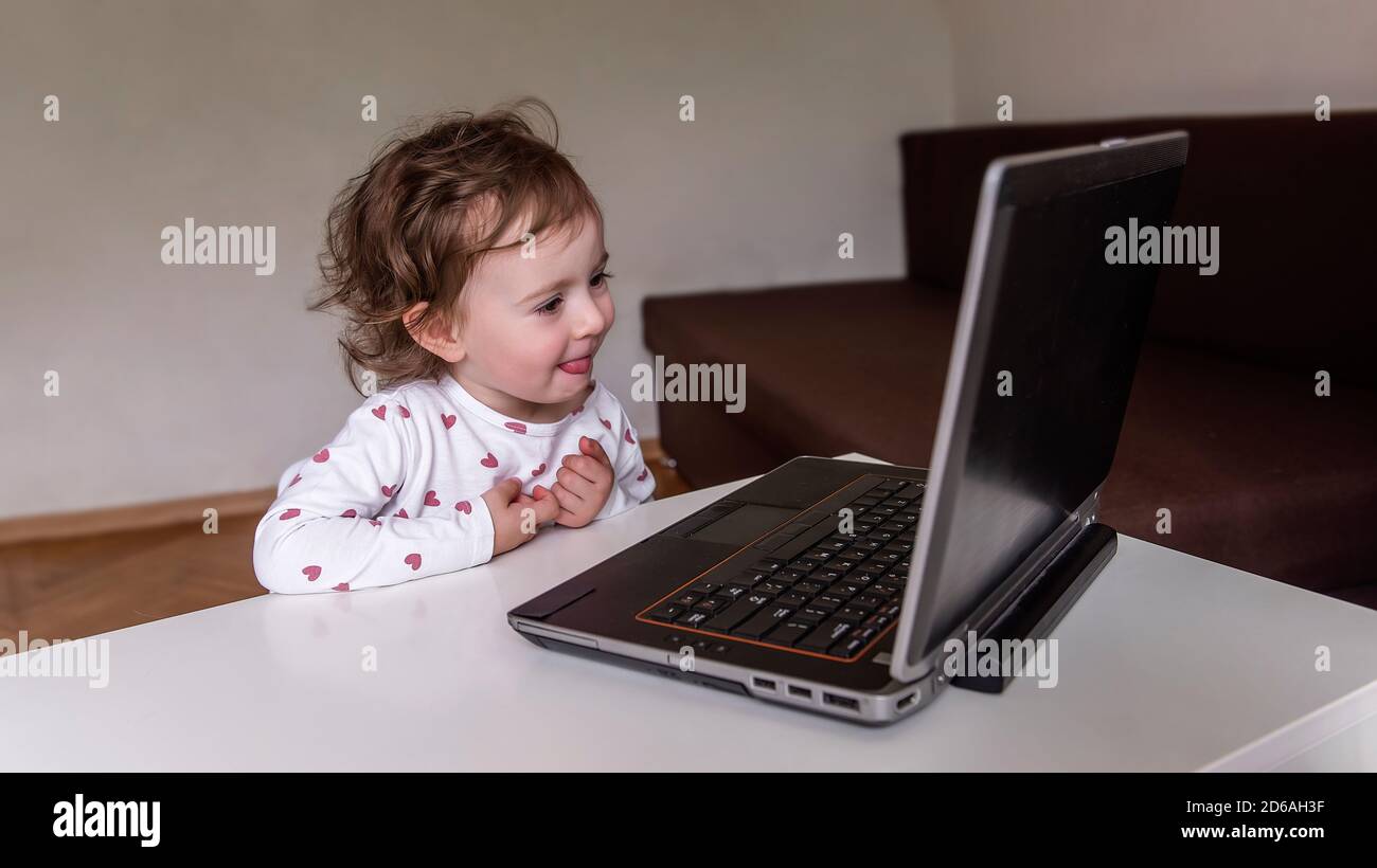 A charming little girl sits behind laptop, learns from distance ...
