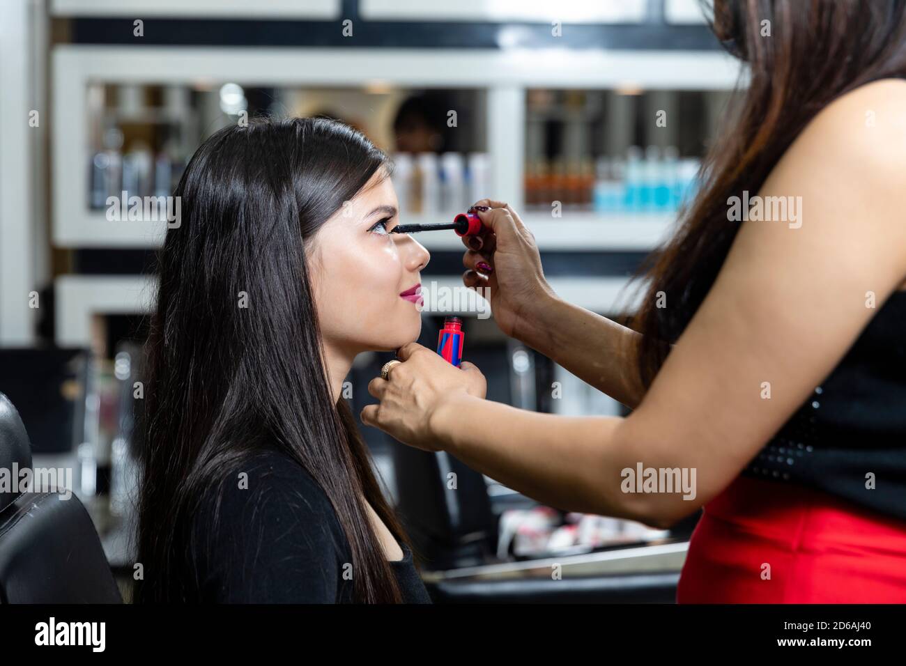 A young Indian model at a beauty salon, makeup artist applying eyeliner ...