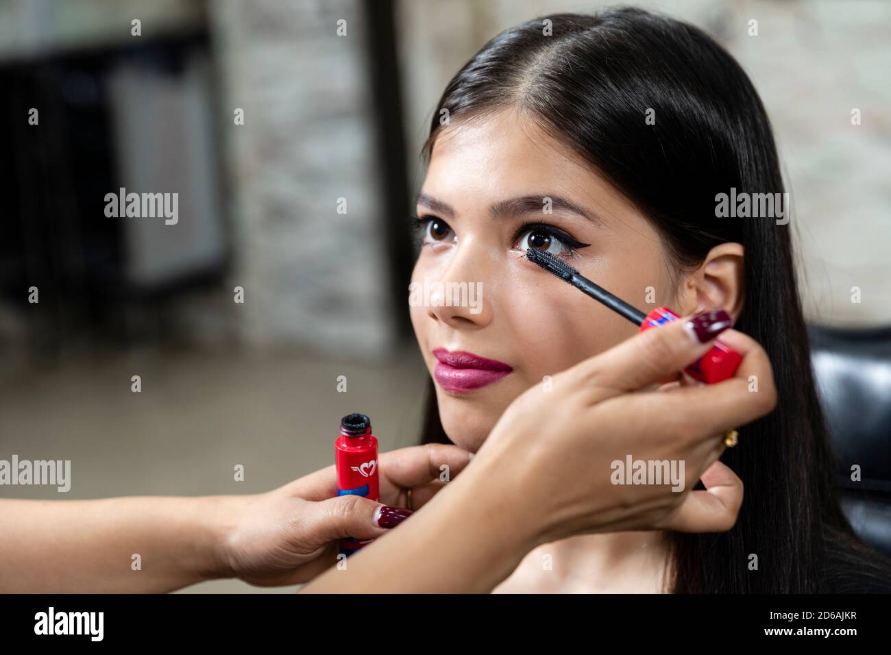 A young Indian model at a beauty salon, makeup artist applying eyeliner ...