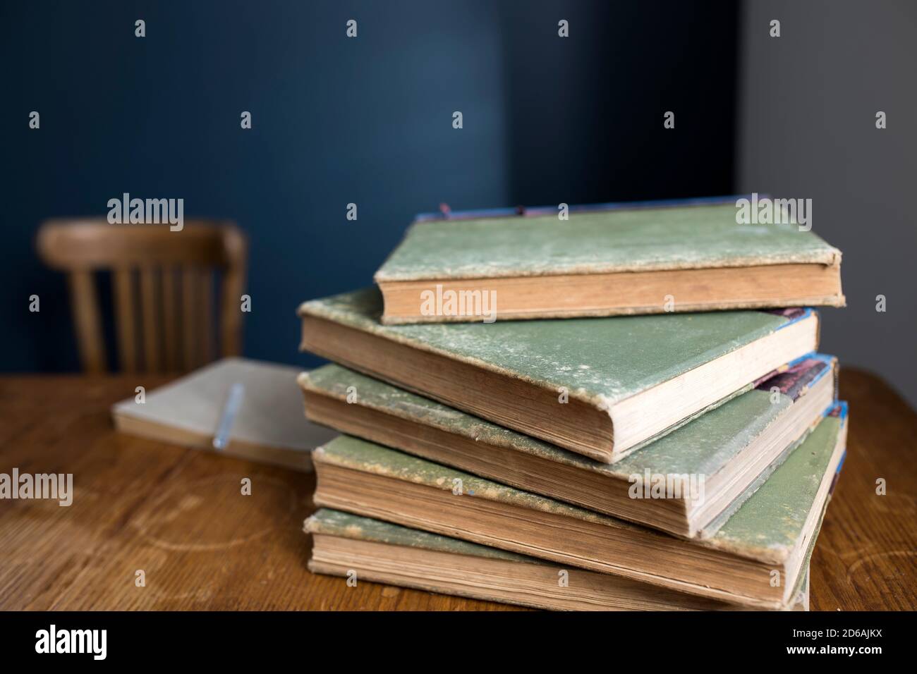 A stack of large, old, rag-bound books lie on a wooden table against a ...