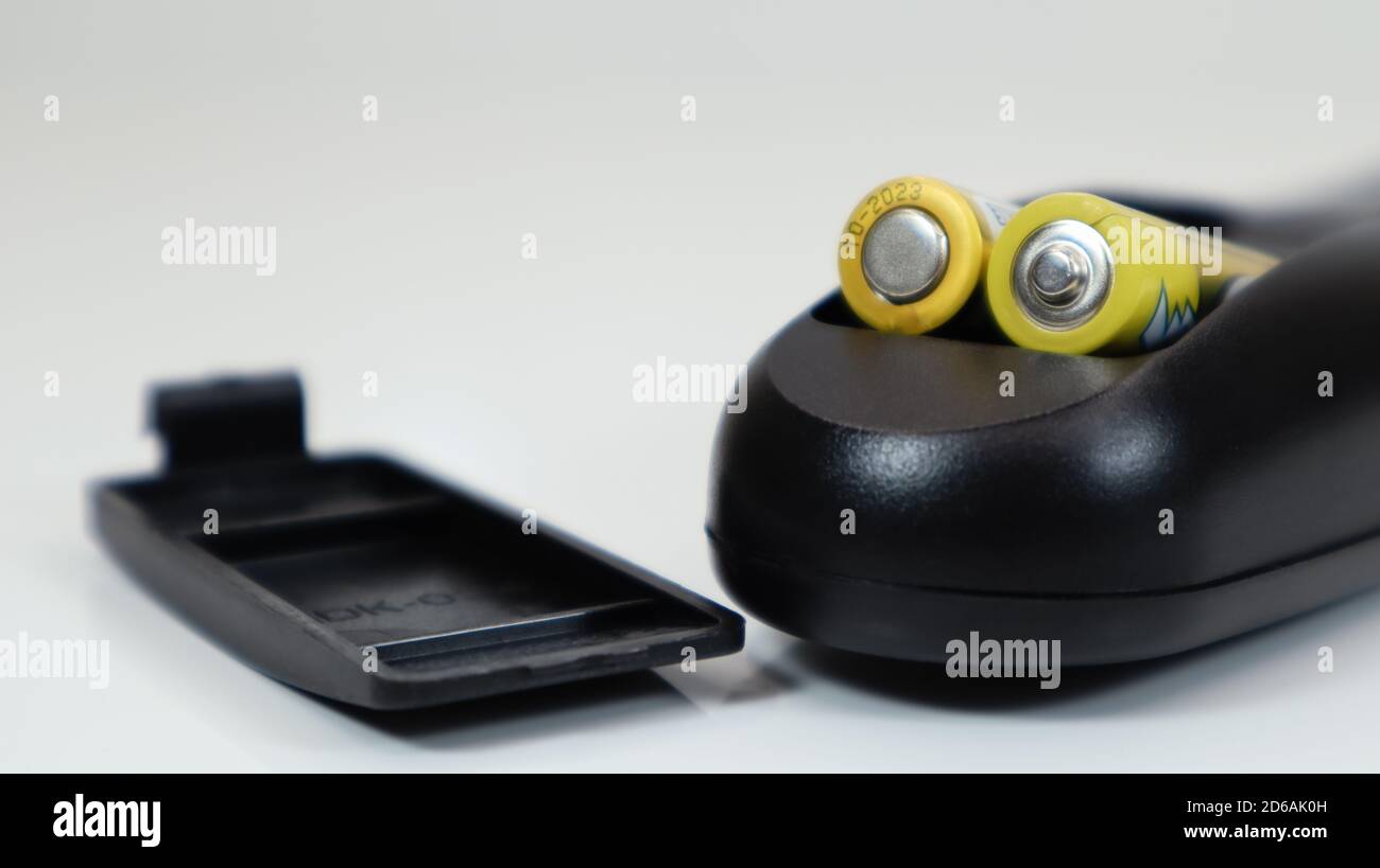 Black remote control with yellow AAA batteries on a white background ...
