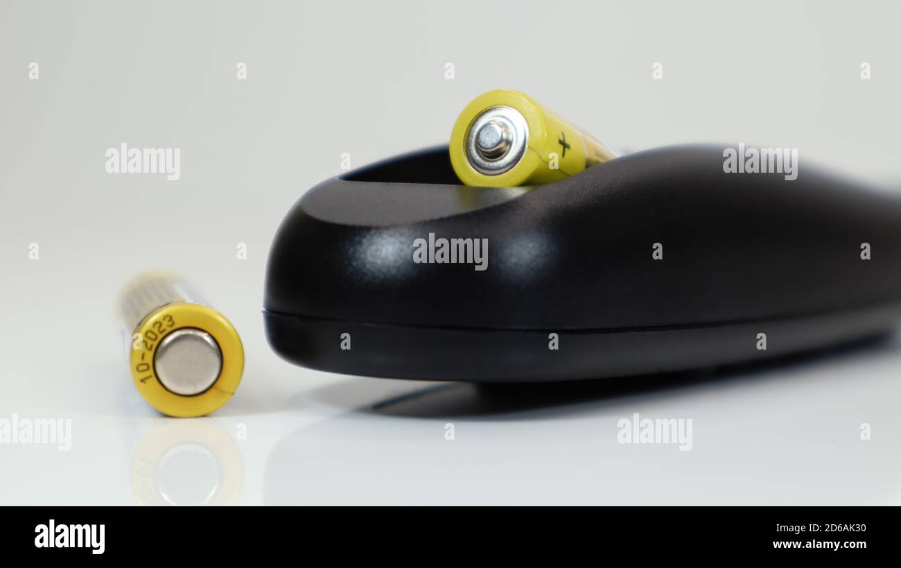 Black remote control with yellow AAA batteries on a white background ...