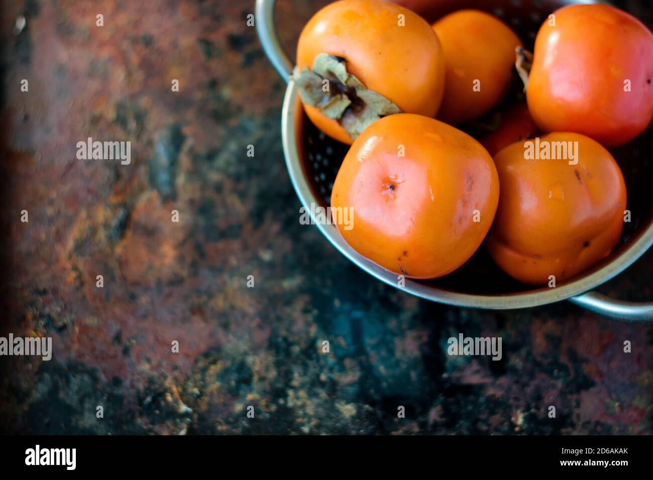 Group of persimmons in metal collander over rustic surface Stock Photo ...