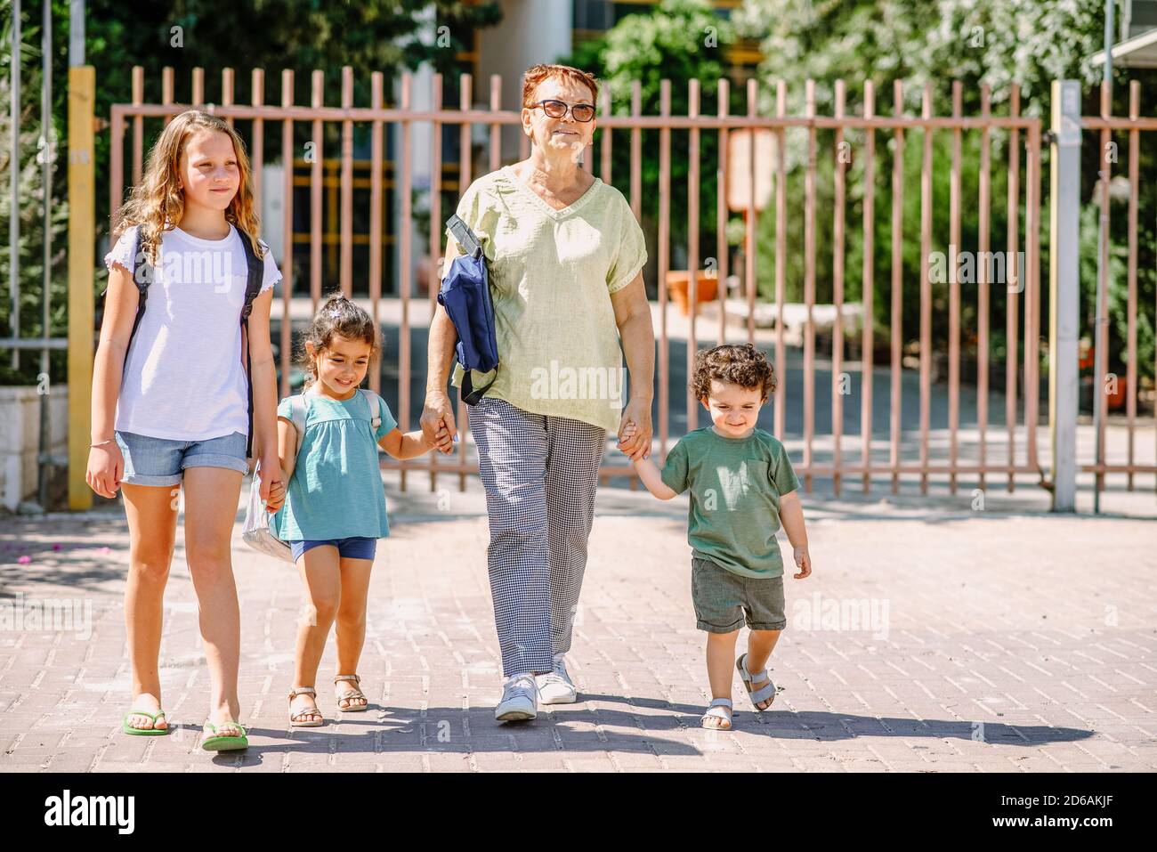 Happy school children going to school with grandmother. Pupils and ...