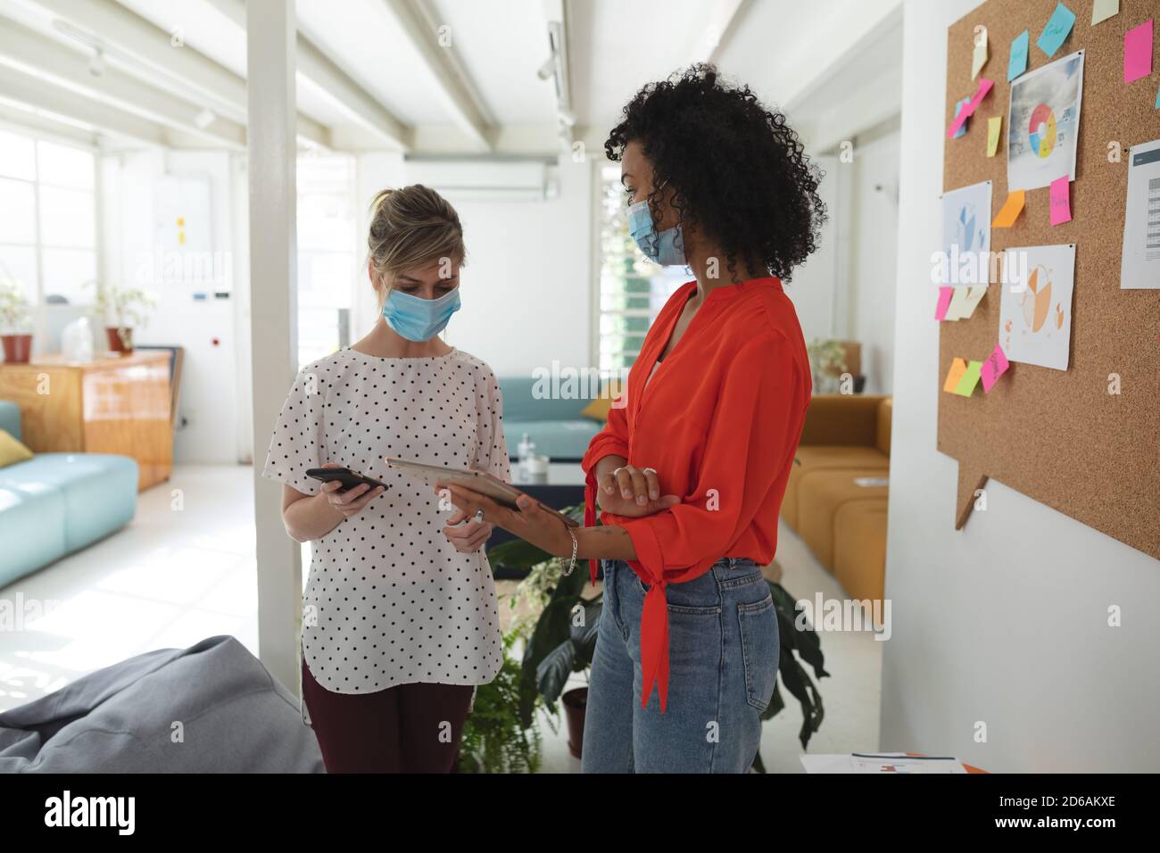 Two woman wearing face masks discussing over a digital tablet at office ...