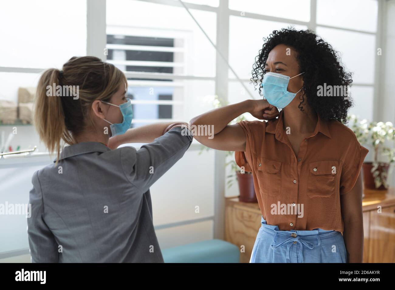 Two woman wearing face masks greeting each other by touching their ...