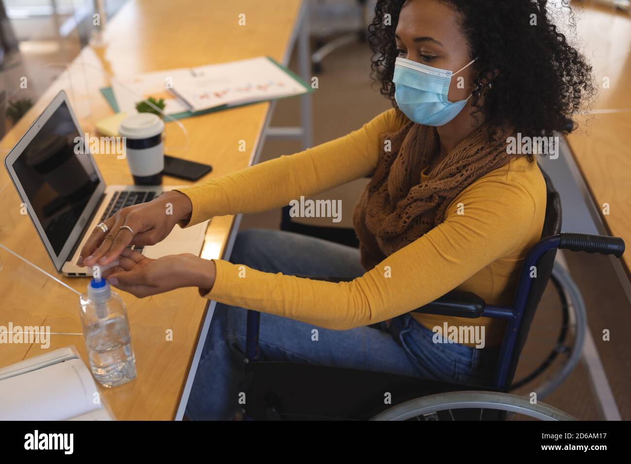 Disable woman wearing face mask sanitizing her hands while sitting on ...