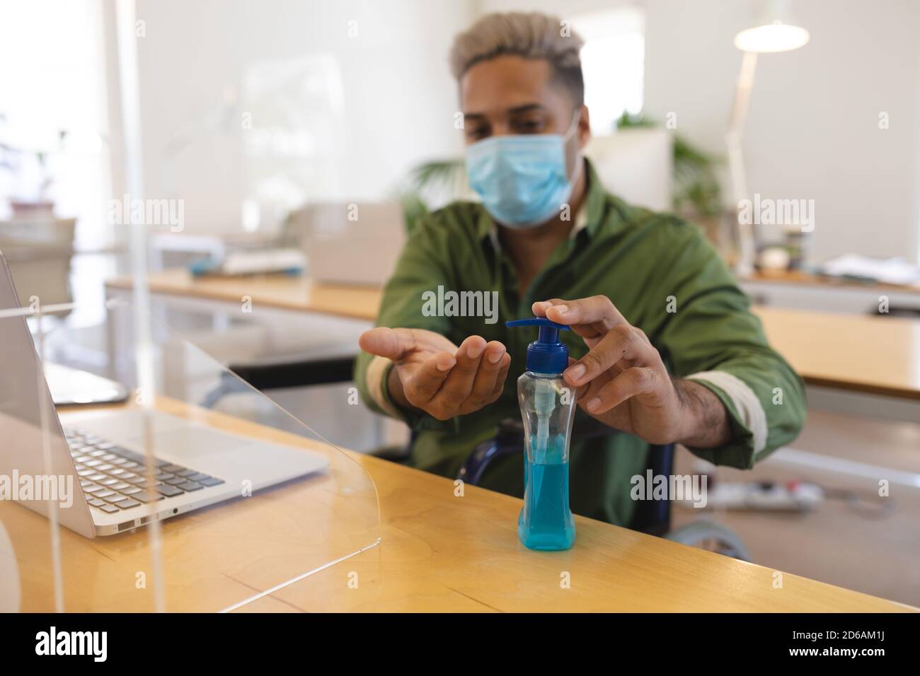 Disable man wearing face mask sanitizing his hands while sitting on his ...