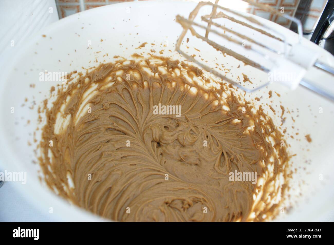 A brown cake batter in a white bowl whisked with a nice pattern and a ...