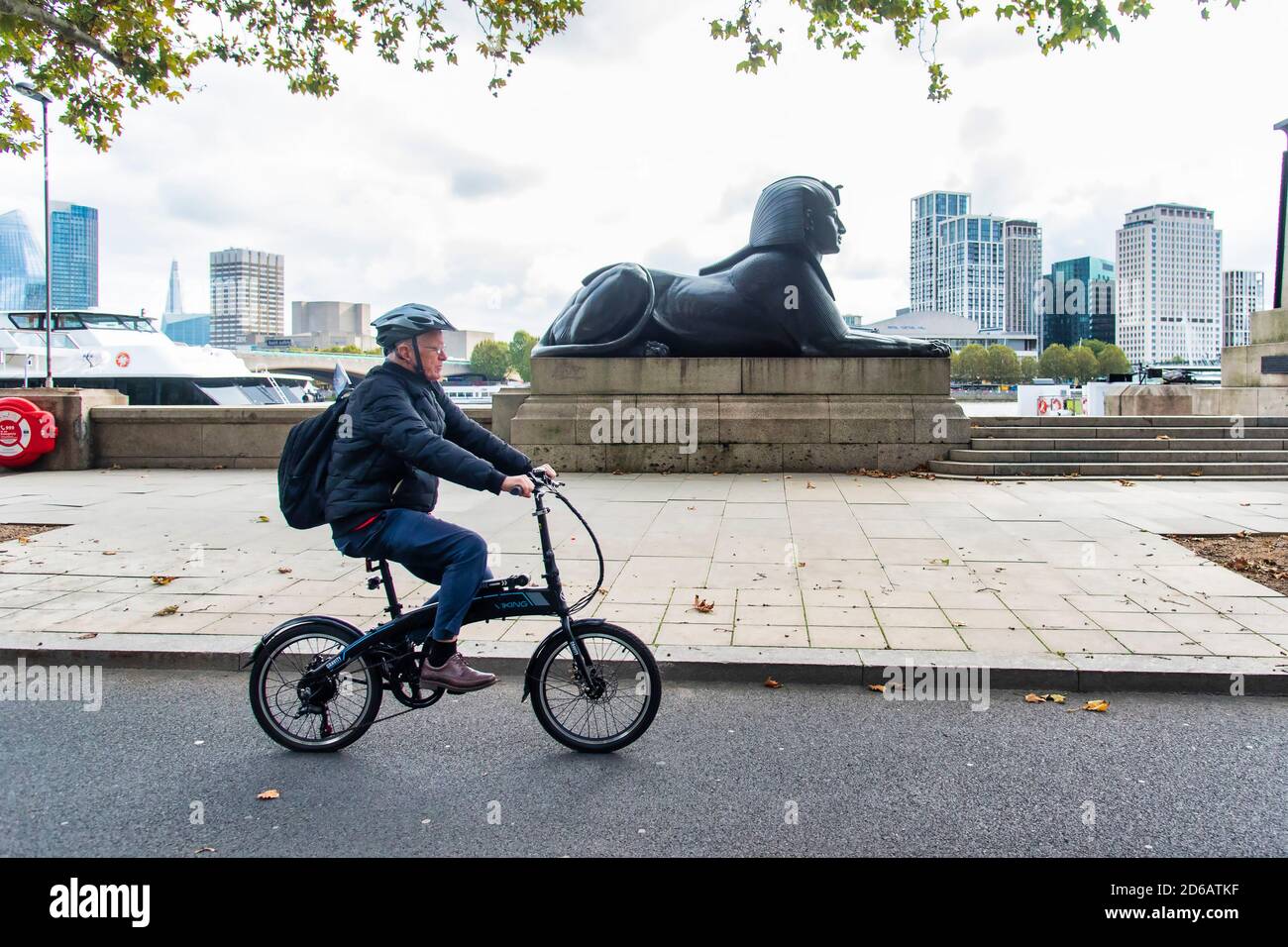 A cyclist on a fold up bike rides past a statue of a Sphinx on London’s ...