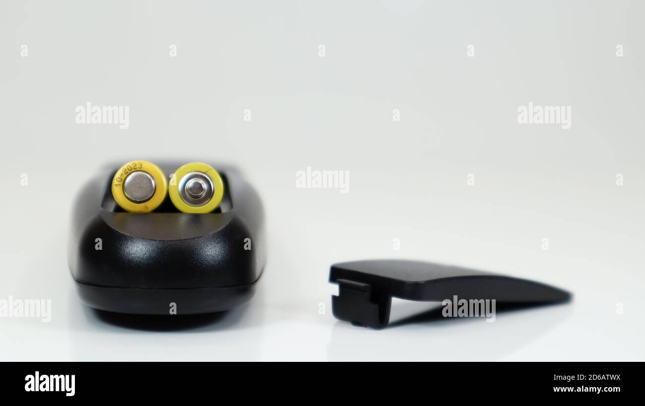 Black remote control with yellow AAA batteries on a white background ...