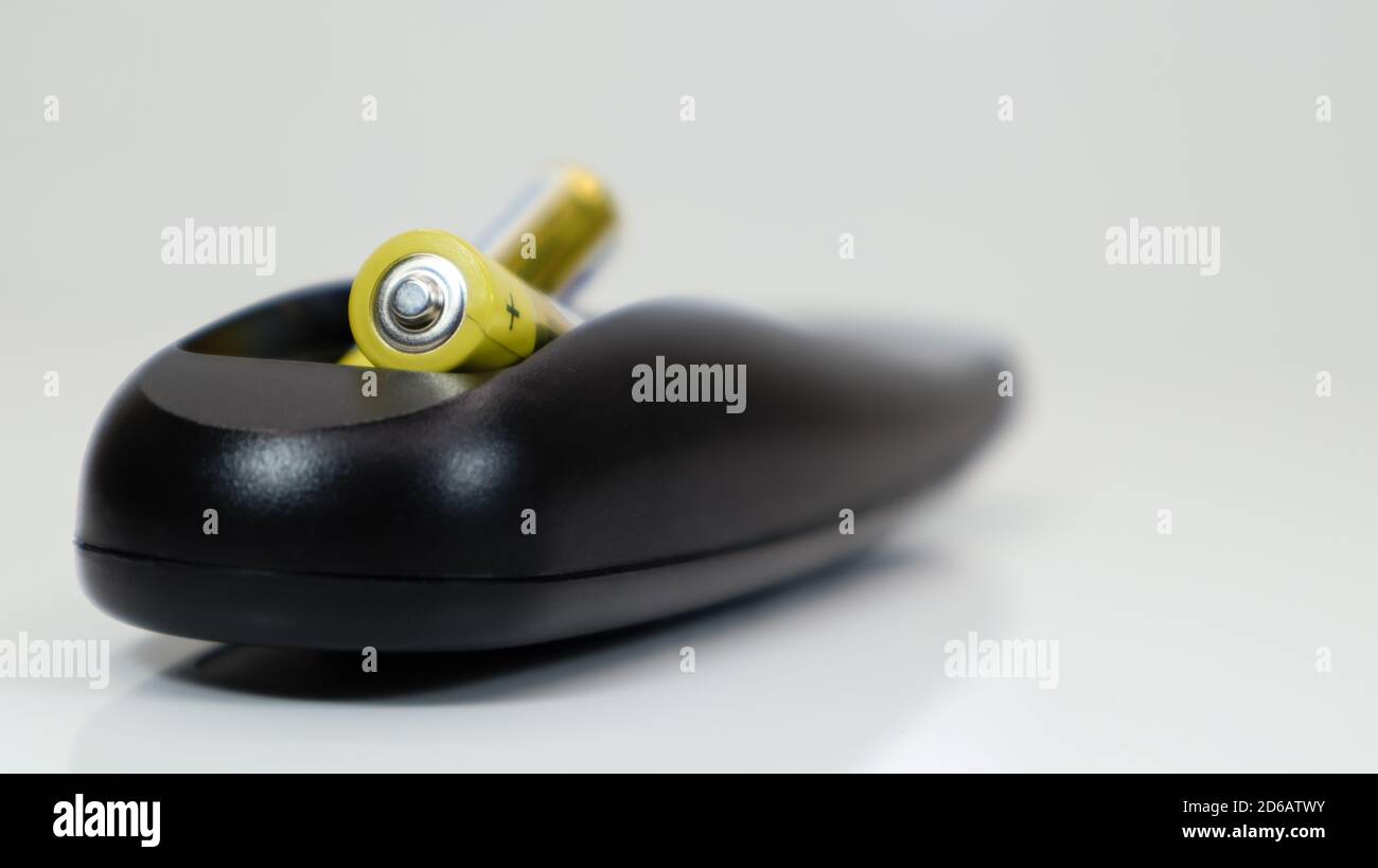Black remote control with yellow AAA batteries on a white background ...