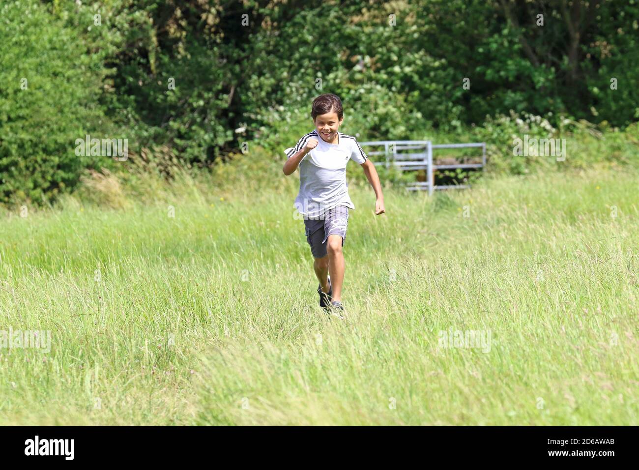 Young boy running across a grassy field in the countryside, laughing ...