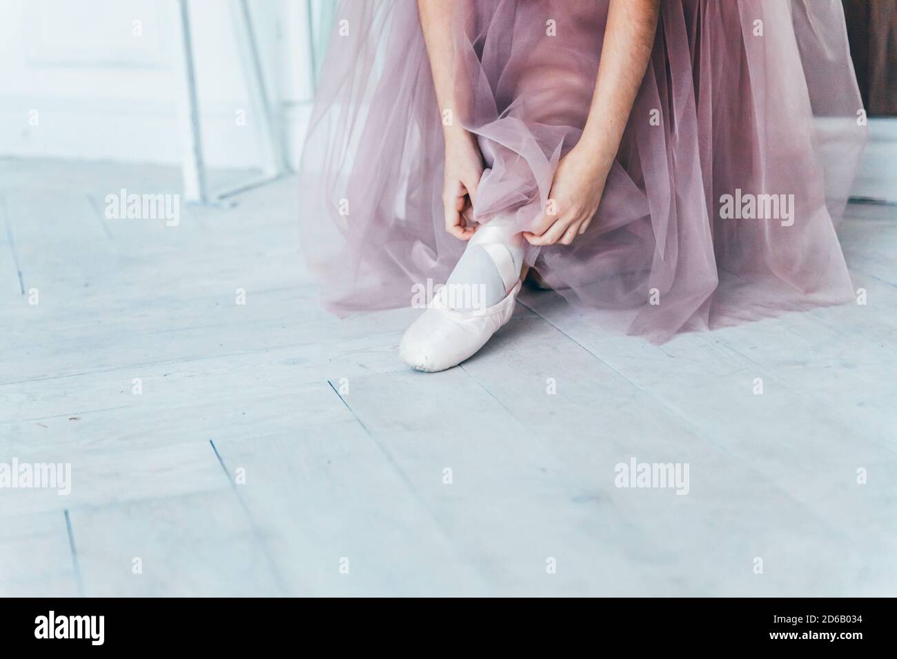 Hands of ballerina in pink tutu skirt puts on pointe shoes on leg in ...