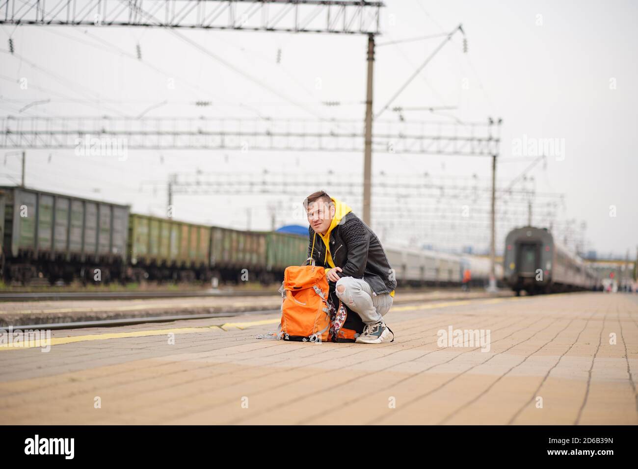 Young man squats on platform, waiting for train. Male passenger with ...