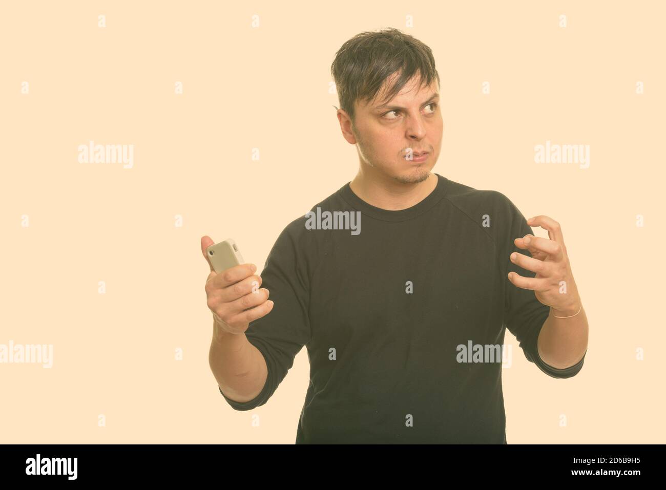 Studio shot of angry man holding mobile phone while thinking Stock ...