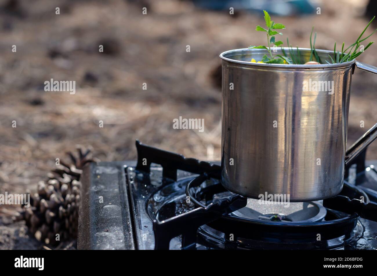 A metal mug with herbal tea on a portable gas stove in the forest ...