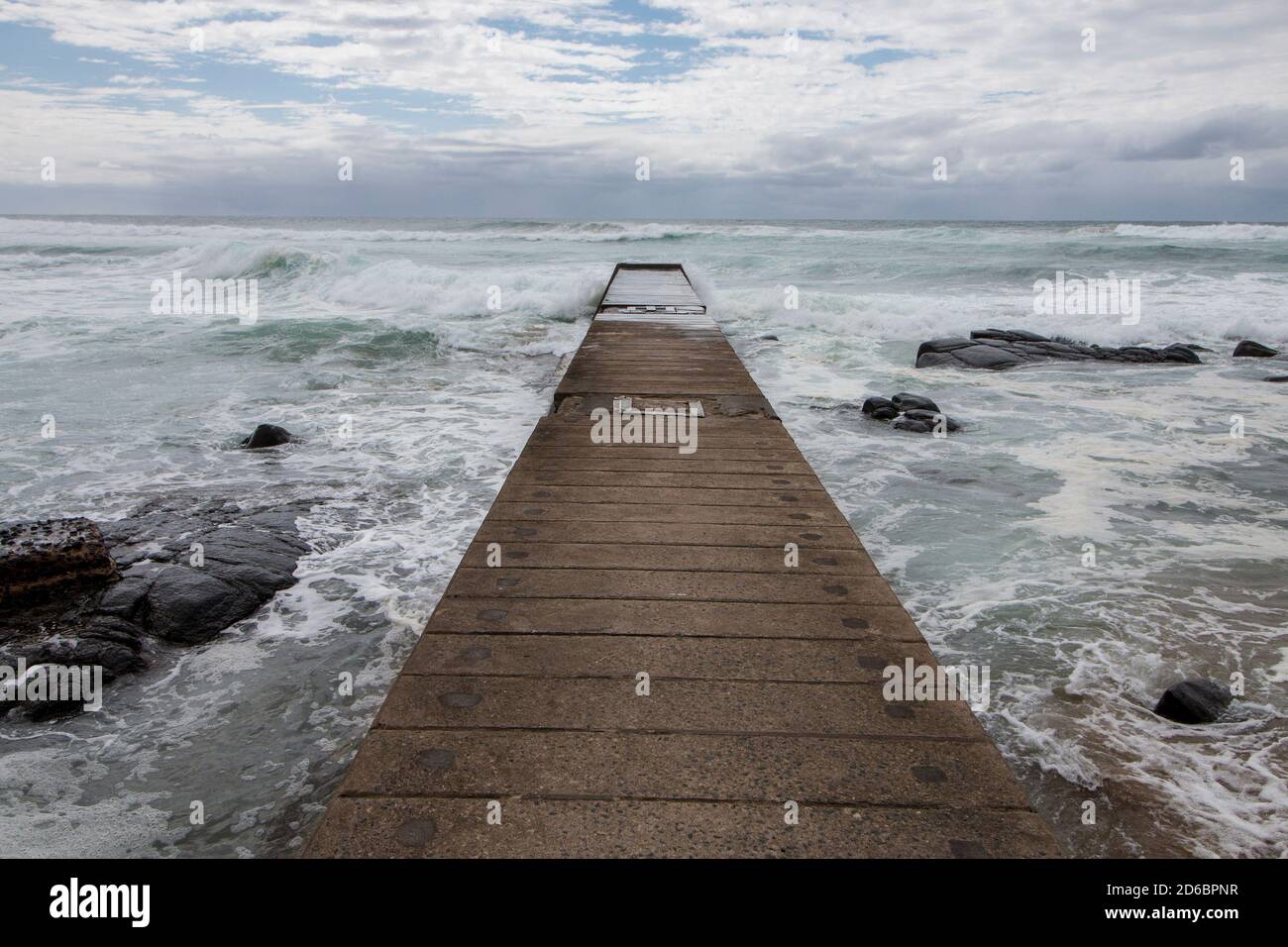 Cement pathway leading into sea surrounded by waves Stock Photo - Alamy