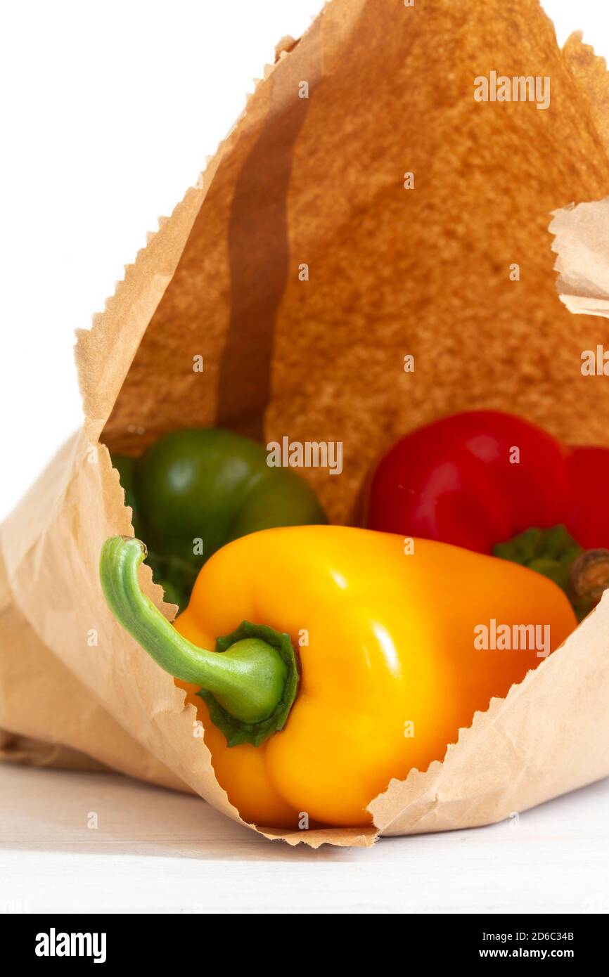 Yellow, red and green peppers in a brown paper bag on a white wood ...