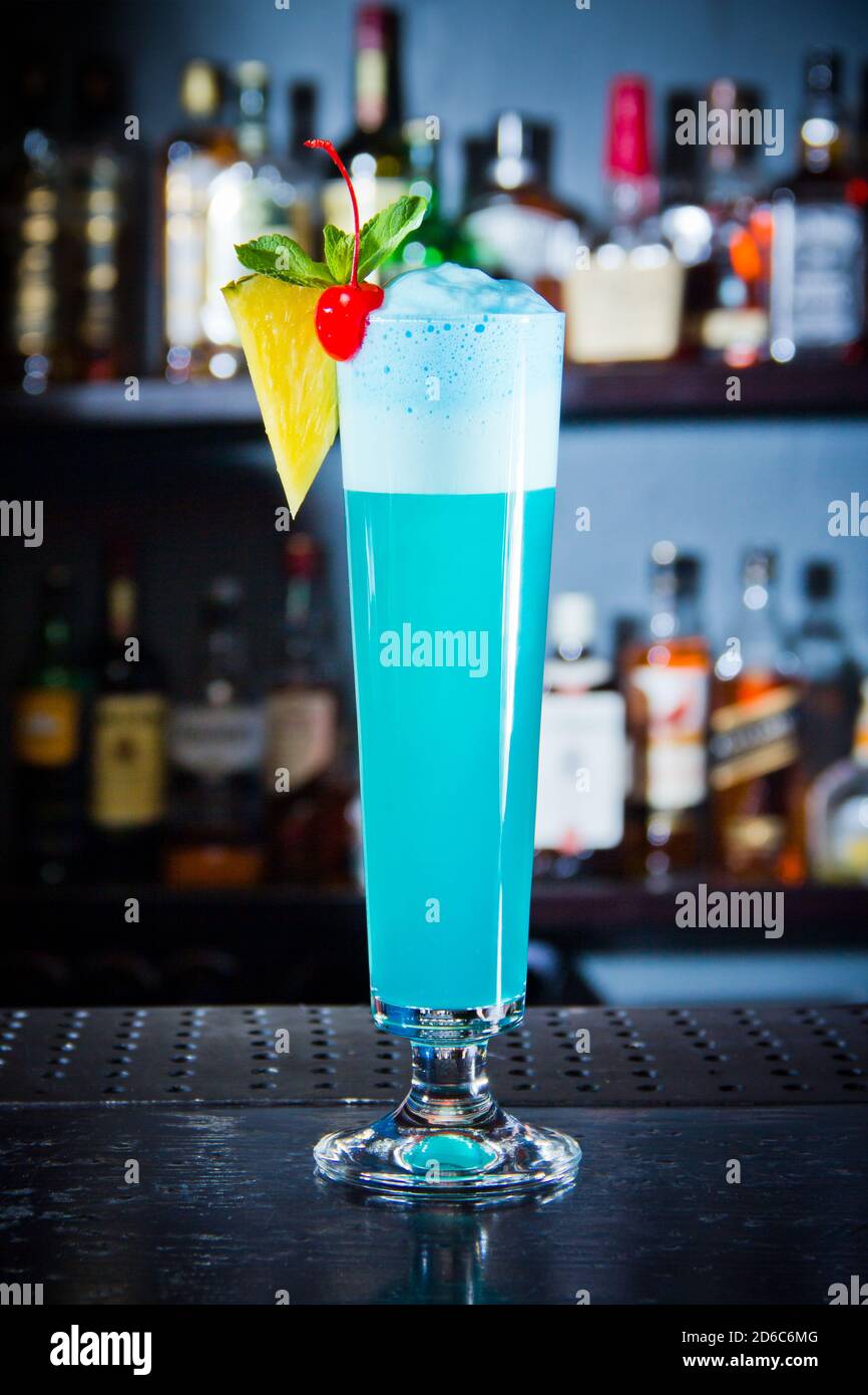 Blue drink cocktail with foam decorated pineapple and cherry in big ...