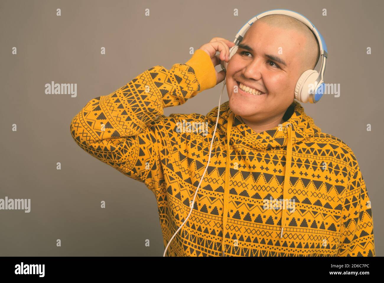 Young bald Asian man listening to music against gray background Stock ...