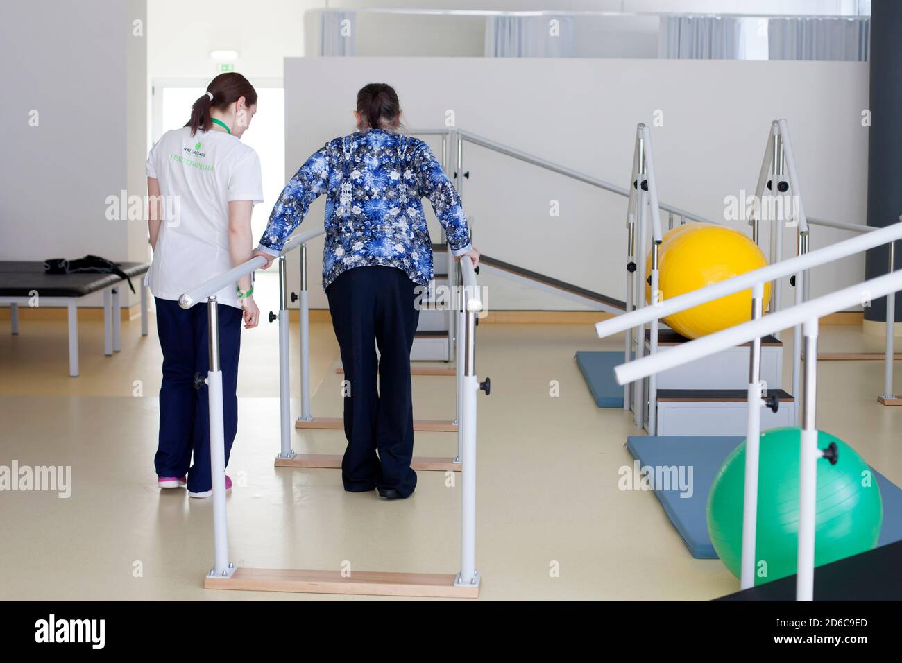 Physiotherapist helping patient walk between parallel bars Stock Photo ...
