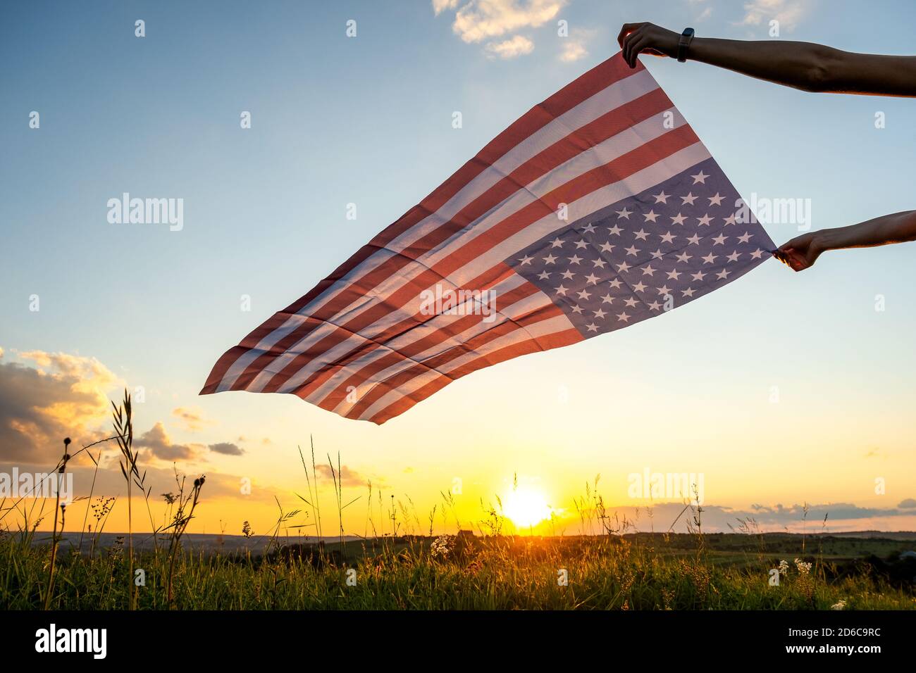 Human hands holding waving american national flag in field at sunset ...