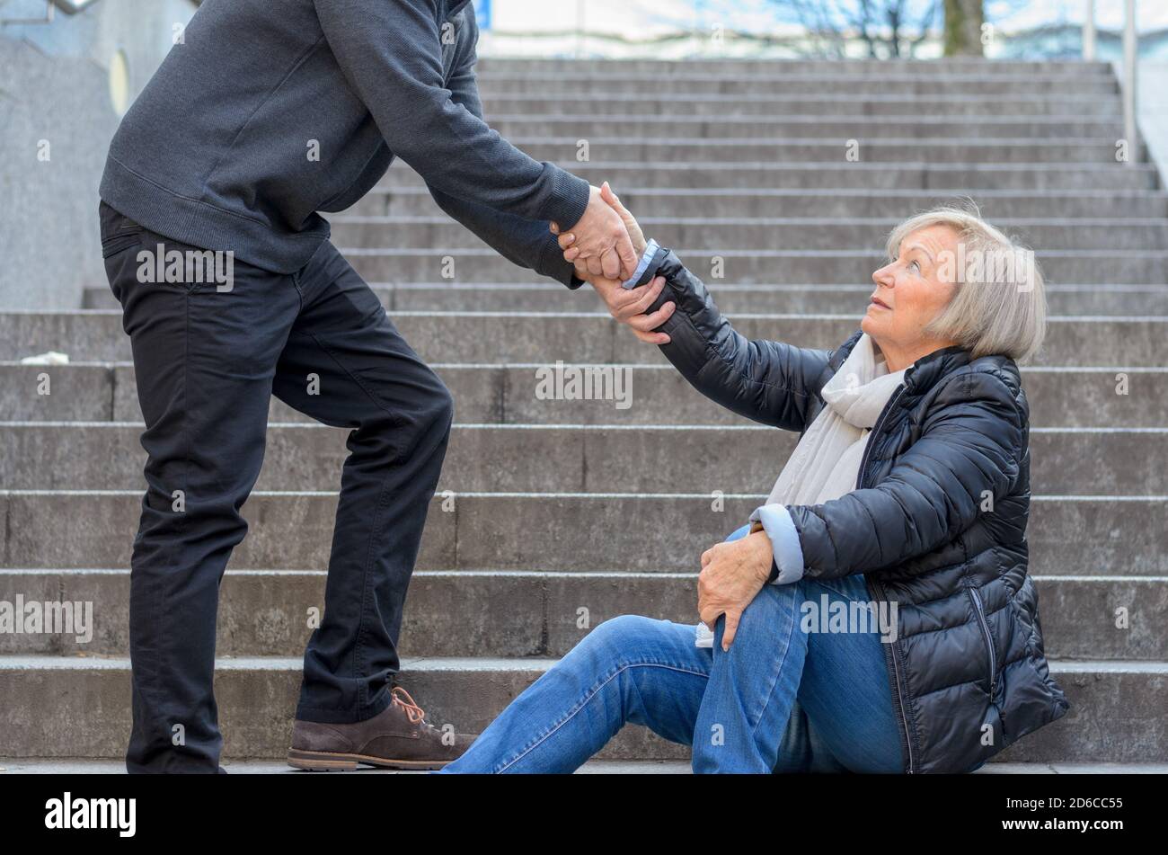 Man helping senior woman to get up while she is sitting on stairs ...