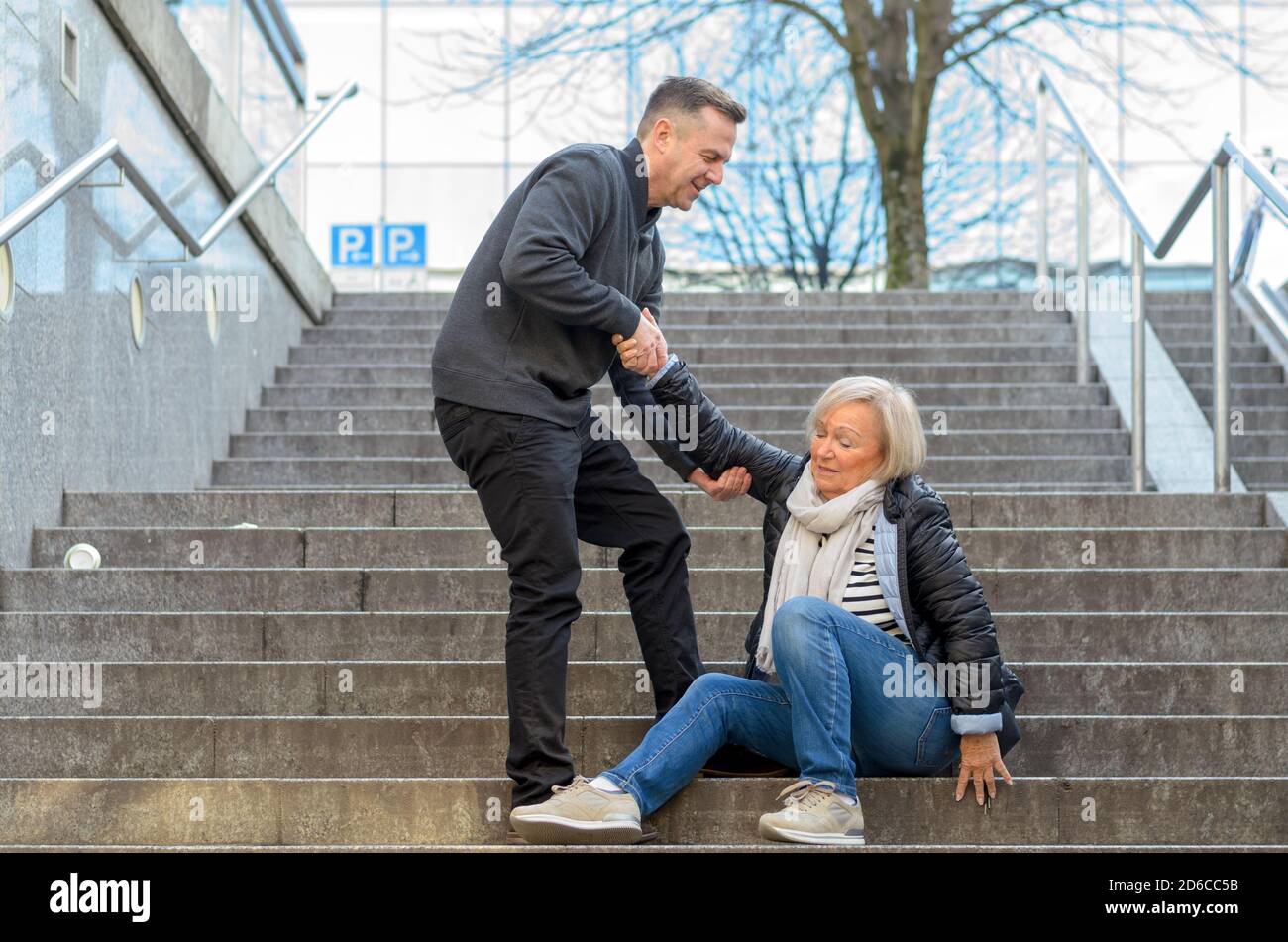Man helping senior woman to get up while she is sitting on stairs ...