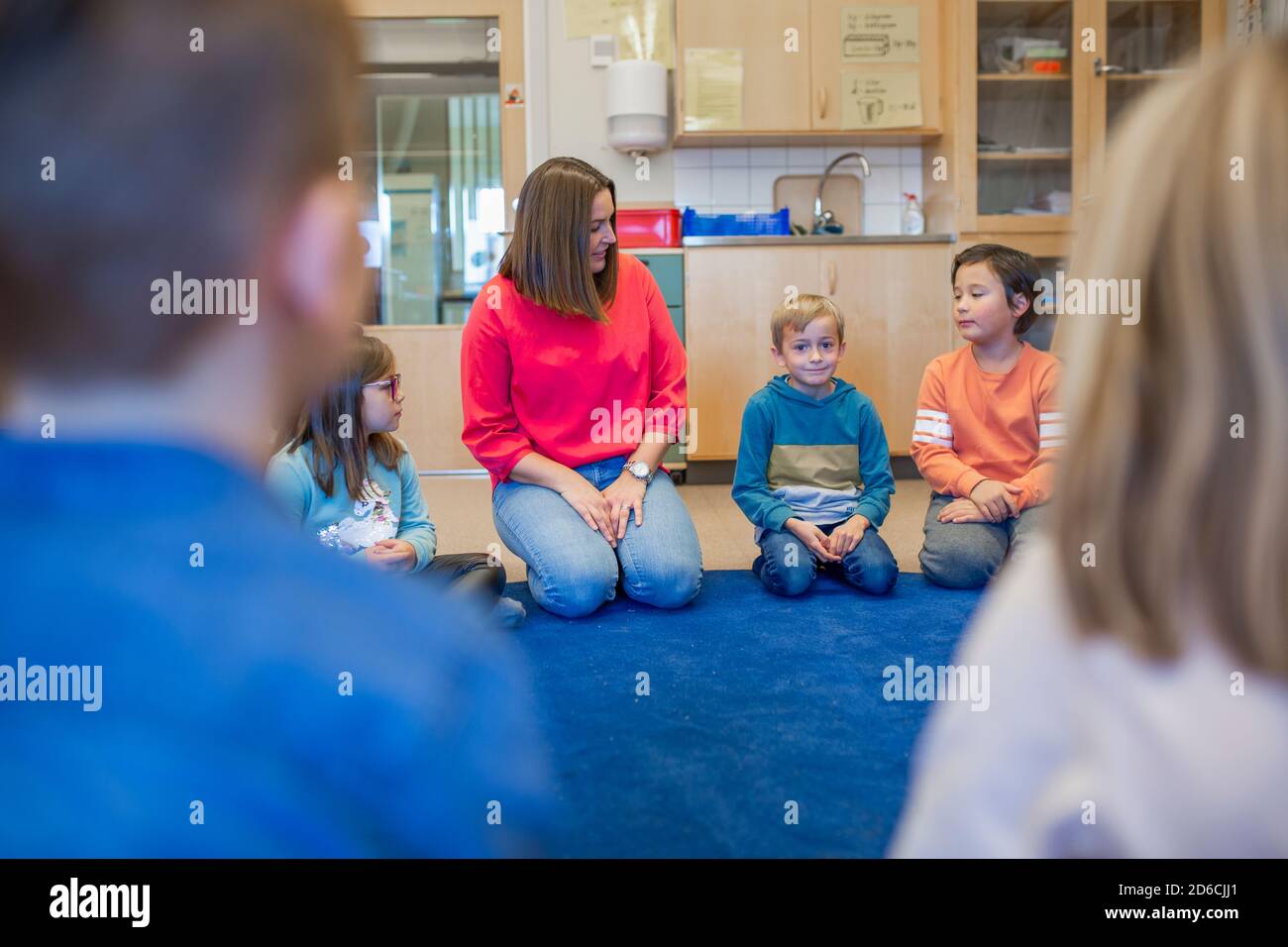 Teacher sitting on floor with children Stock Photo - Alamy