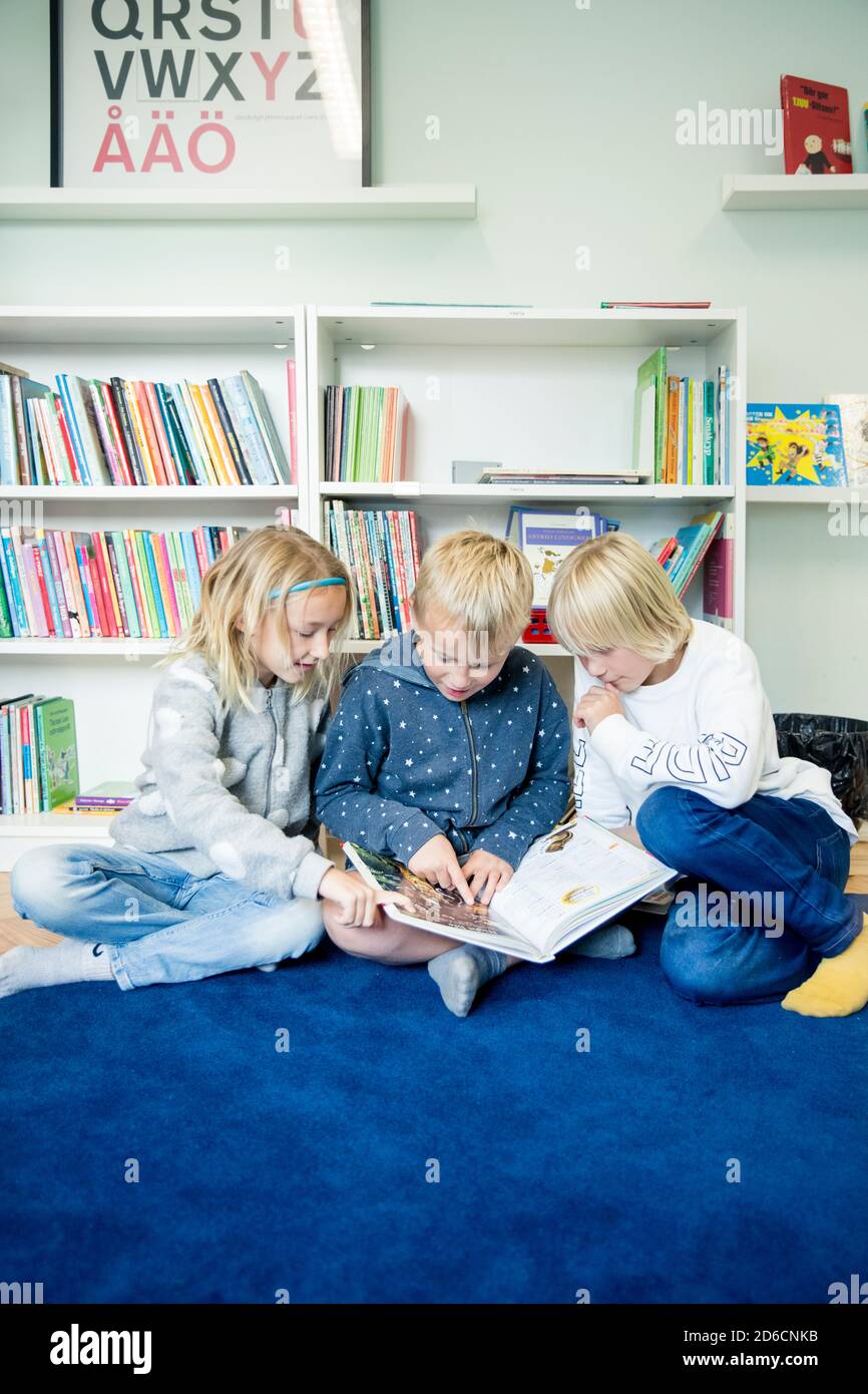 Kids looking at book together Stock Photo - Alamy