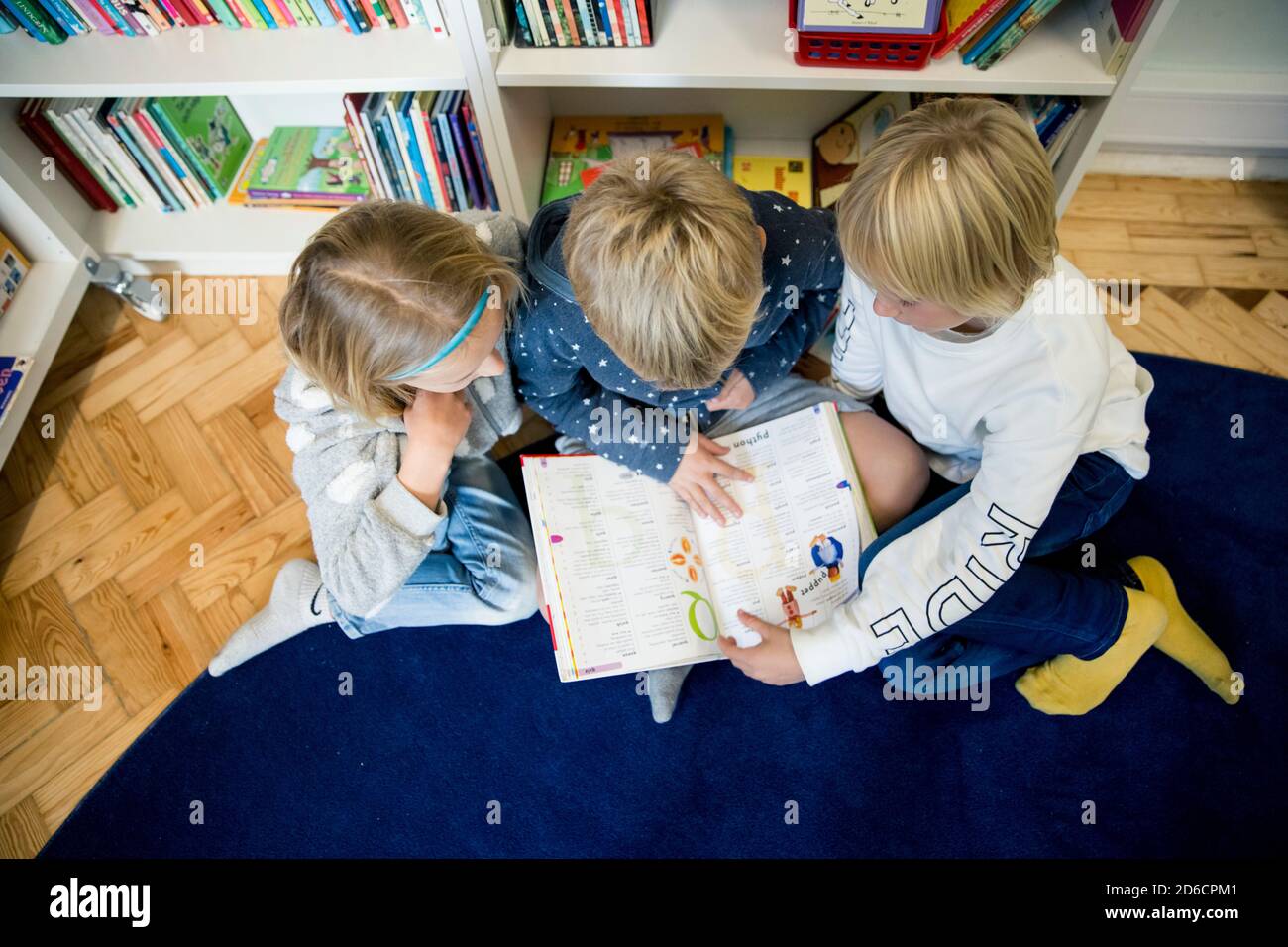Kids looking at book together Stock Photo - Alamy