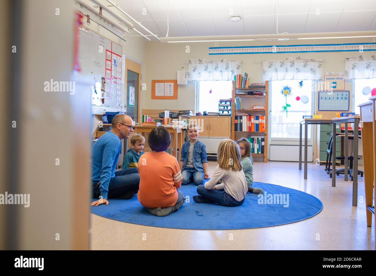 Teacher sitting on floor with children Stock Photo - Alamy