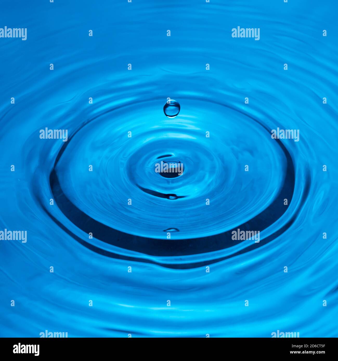 Water drop falling into water making a perfect droplet splash in blue ...