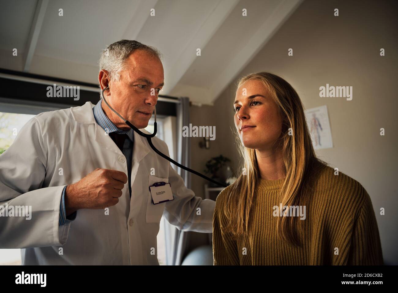 Elderly doctor listening to heart beat of sick female patient sitting ...