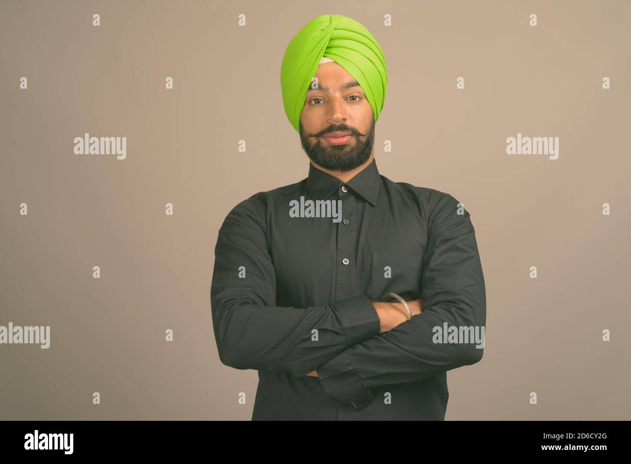 Young handsome Indian Sikh businessman wearing turban against gray ...