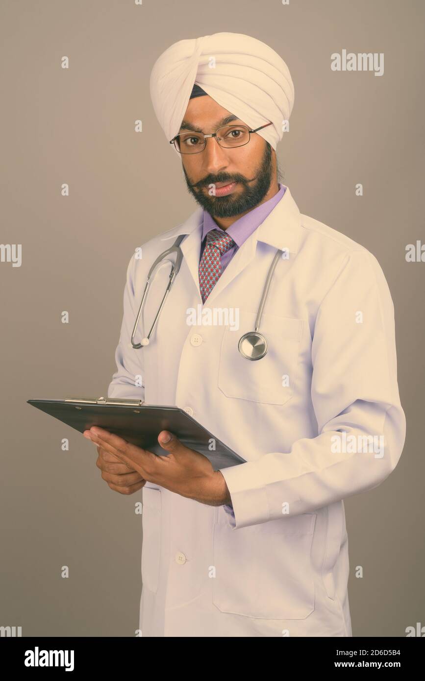 Young handsome Indian Sikh man doctor against gray background Stock ...