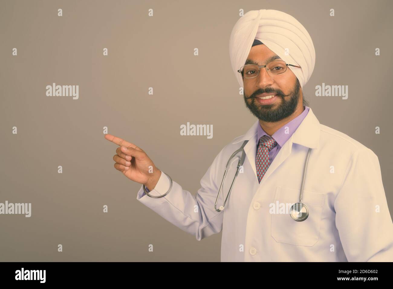 Young handsome Indian Sikh man doctor against gray background Stock ...