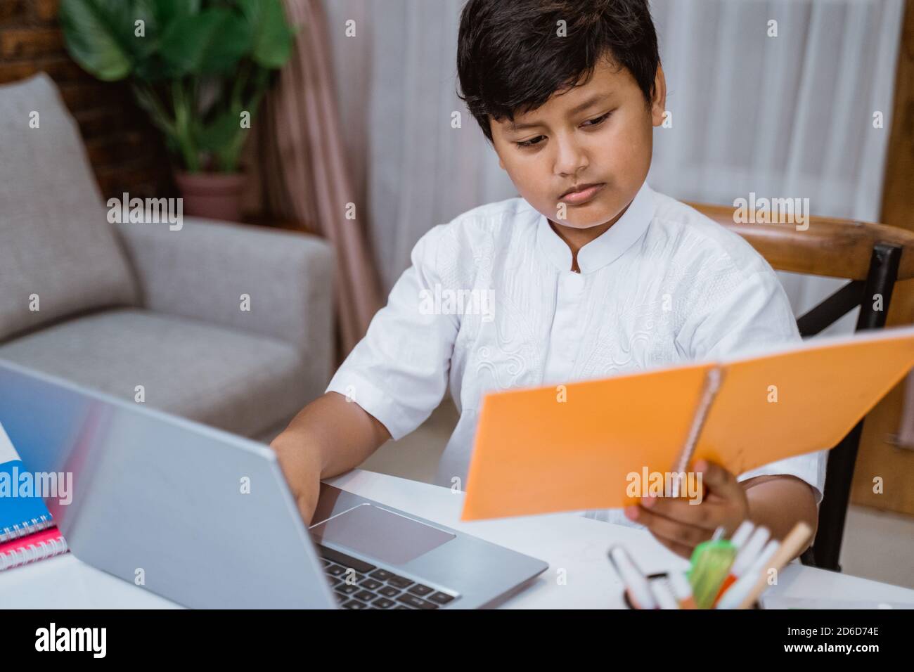 a boy doing homework at home with laptop and writing notes Stock Photo ...